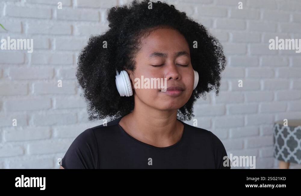 Afro woman with a cute expression, with her eyes closed, listens to ...