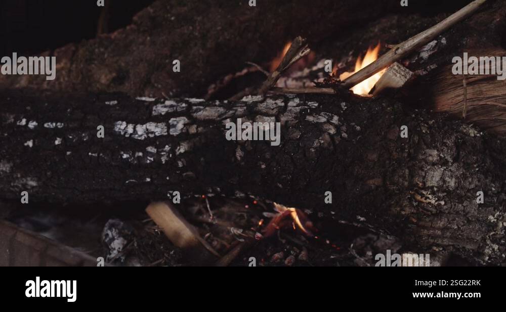 A small log fire going out with burnt remains and small flames, hand ...