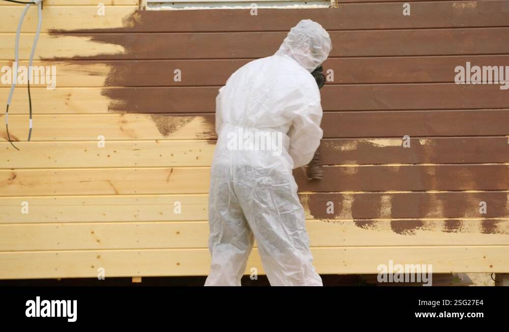 Man painter in protective suit is painting wood facade wall using ...