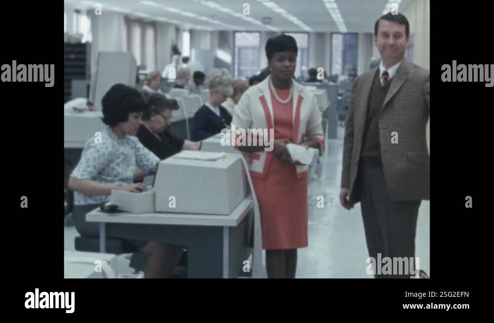 1960s: Busy office, women type on adding machines. Man holds microphone ...