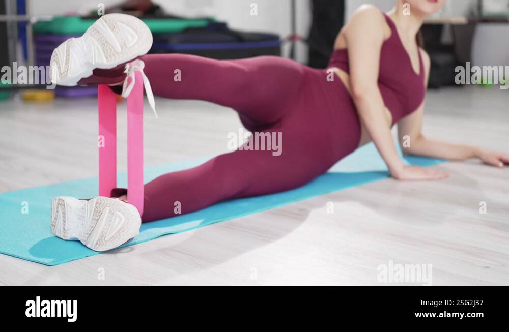 woman in a tracksuit does leg exercises with gymnastic elastic bands on ...