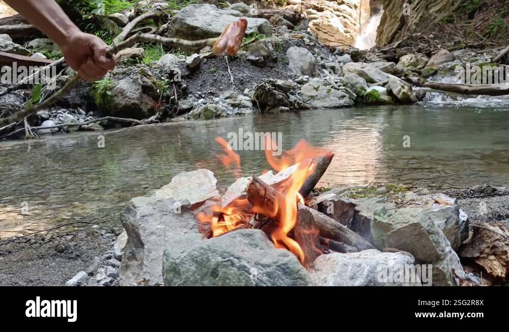 Guy takes well done sausages from camp fire to eat next to river Stock ...