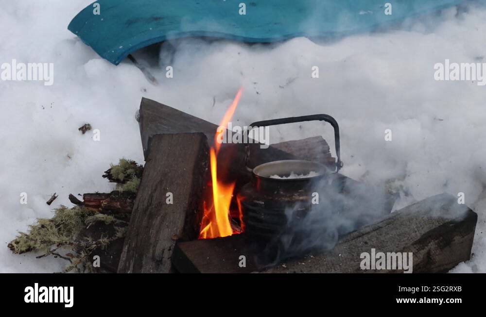 A traditional Australian billy boiling water over a fire in the snow of ...