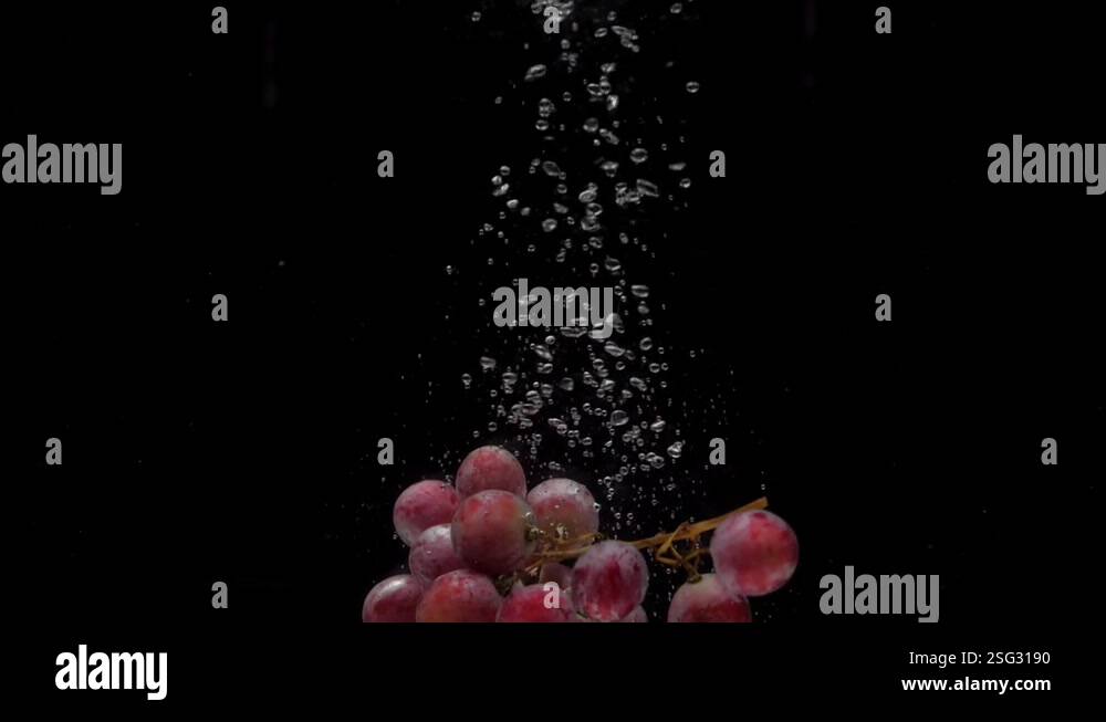 Slow motion red grapes falling into transparent water on black ...