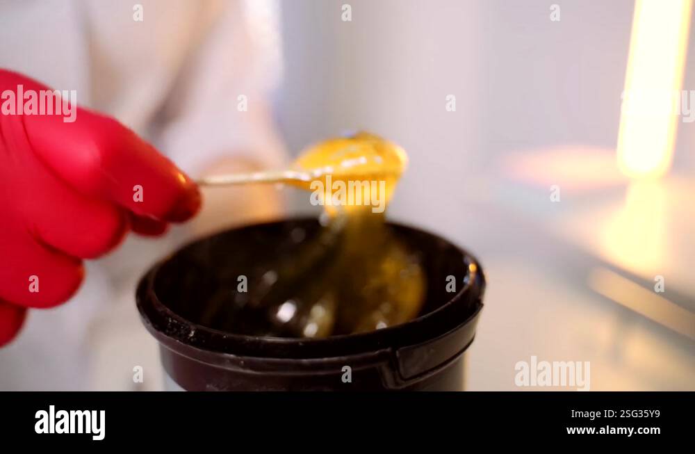Handyman in red gloves stirs sugar paste before removing unwanted hair ...