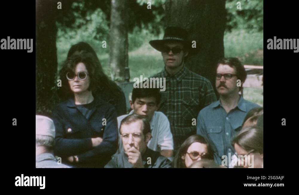 1970s: man with 1970s haircut and beard. Crowd watches blacksmith ...