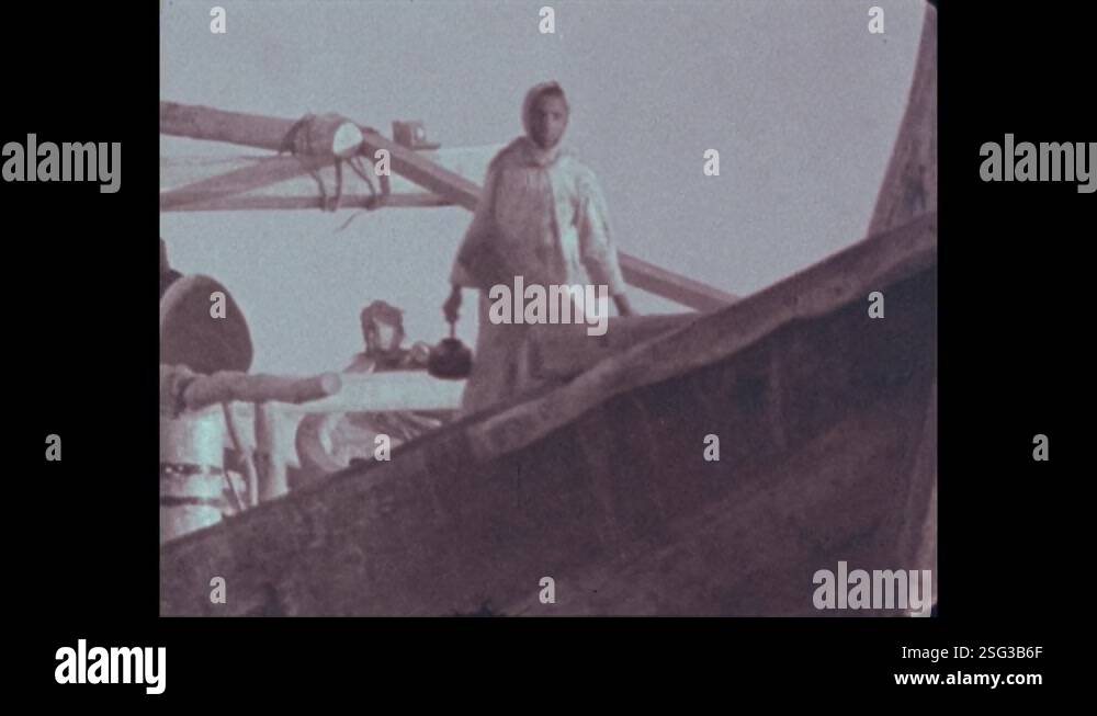 1980s: Men on the deck of a large wooden ship. Sun setting behind rocky ...