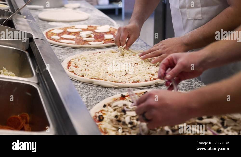Restaurant cooks simultaneously topping pizzas with cheese and ...