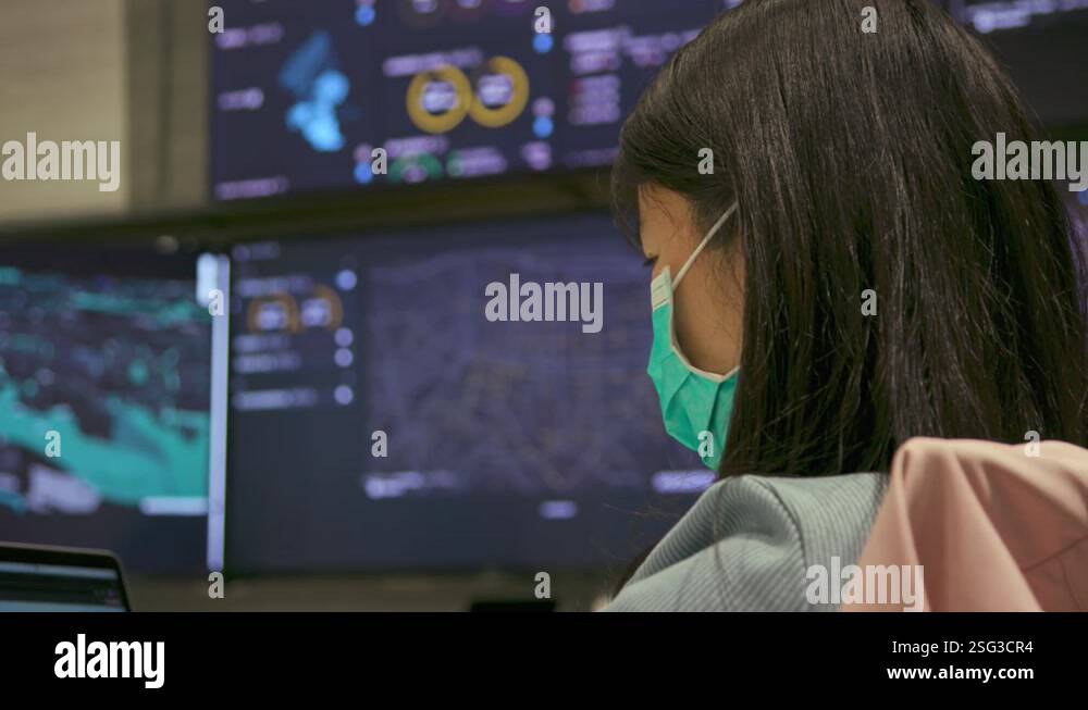 Asian woman wearing a mask working on a computer with giant screens in ...