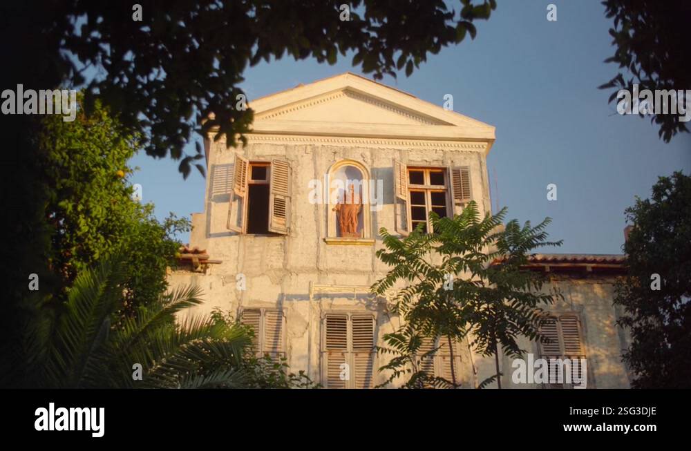 Ancient greek house with a statue on the wall, framed by lush leaves ...