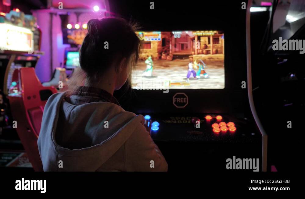 Back view: woman pushing buttons and playing fighting game arcade ...