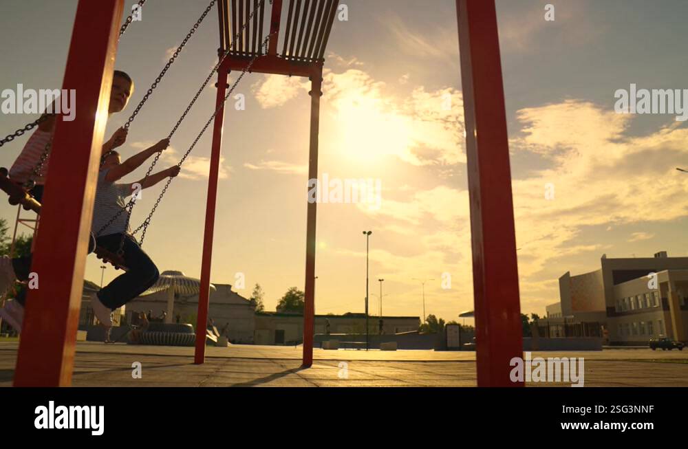 Children swing on swing in city park, sun. Boys play on swings ...