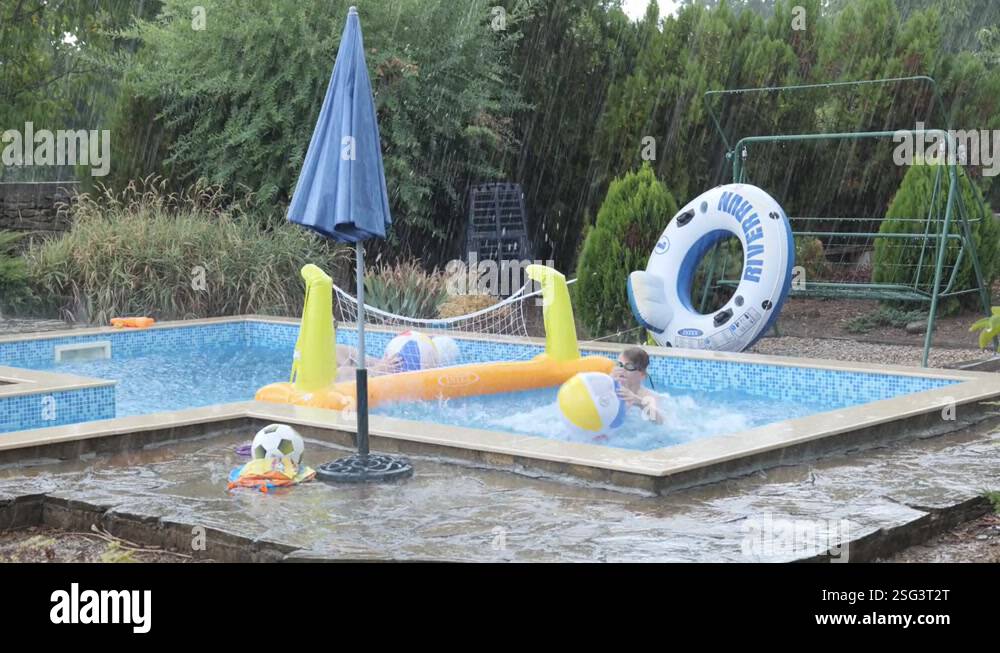 Boy jumps playfully into garden swim pool in heavy rain storm Stock ...