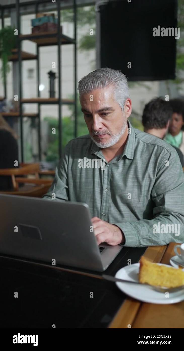 Older entrepreneur seated at coffee shop with laptop staring at screen ...