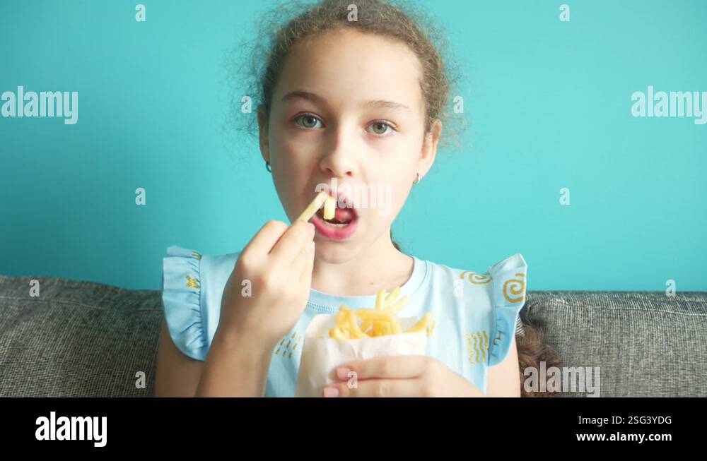 Child eat french fries on blue background.. Cute little girl licks her ...