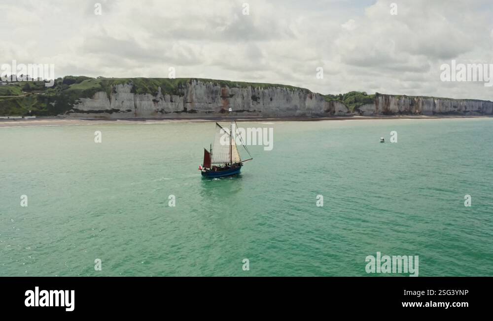 A sailing tourist ship sails along picturesque sheer cliffs with ...