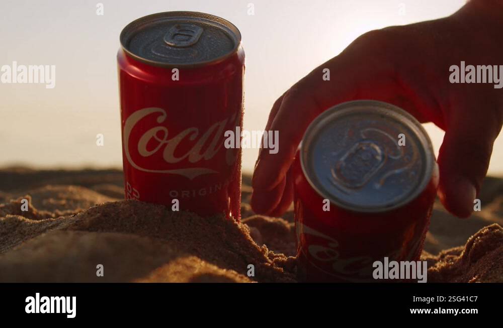 Two tin cans of Coca Cola on a sandy beach with a beautiful sunrise ...