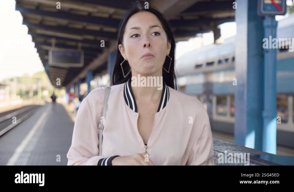 A young beautiful Caucasian woman eats a snack as she waits for a train ...