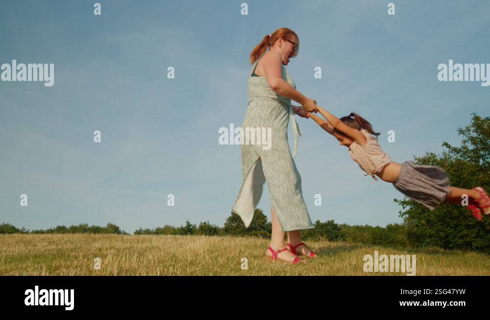 Mom holds her daughter by the hands and rotates her in a circle in the ...