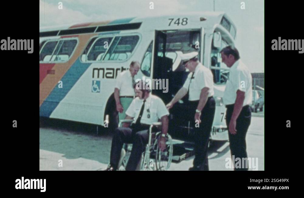 1980s: Man standing by bus facility signage, talking. Men talking at ...