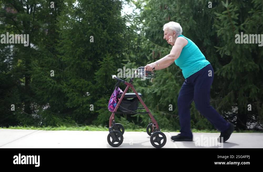 Elderly senior woman pushing a walker, rolling it on a sidewalk outside ...