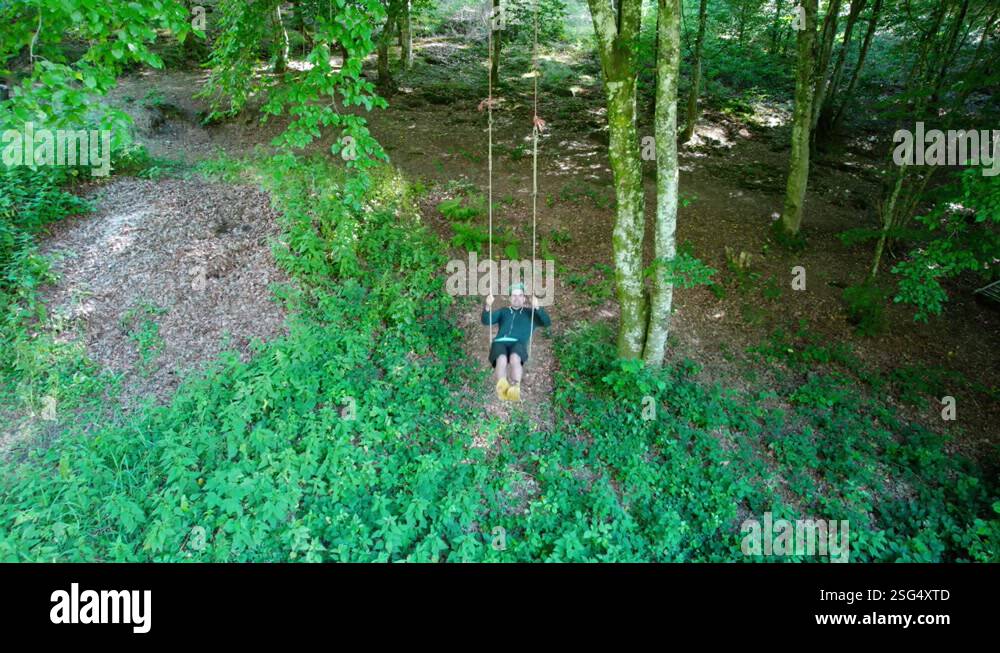 young adult on giant swing in forest seen from above in overview shot ...