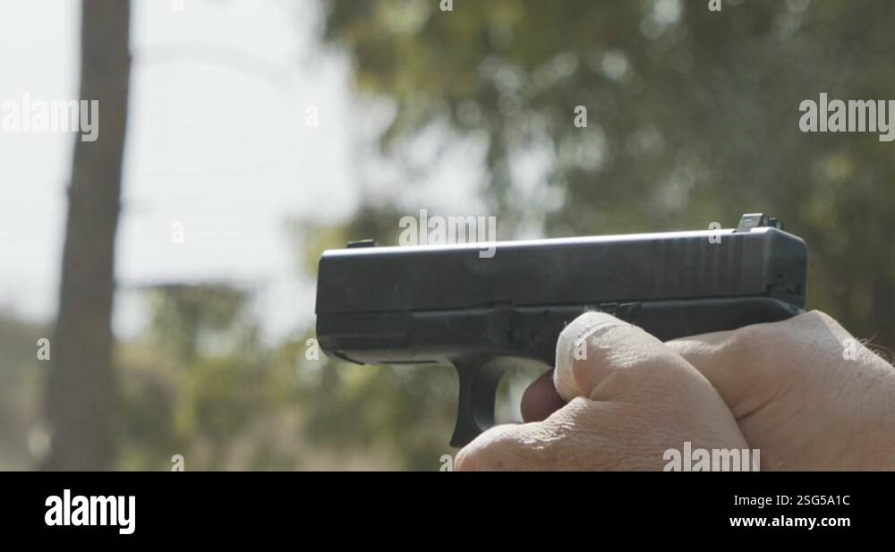 Slow motion of a man firing a hand gun in a firing range with cartridge ...