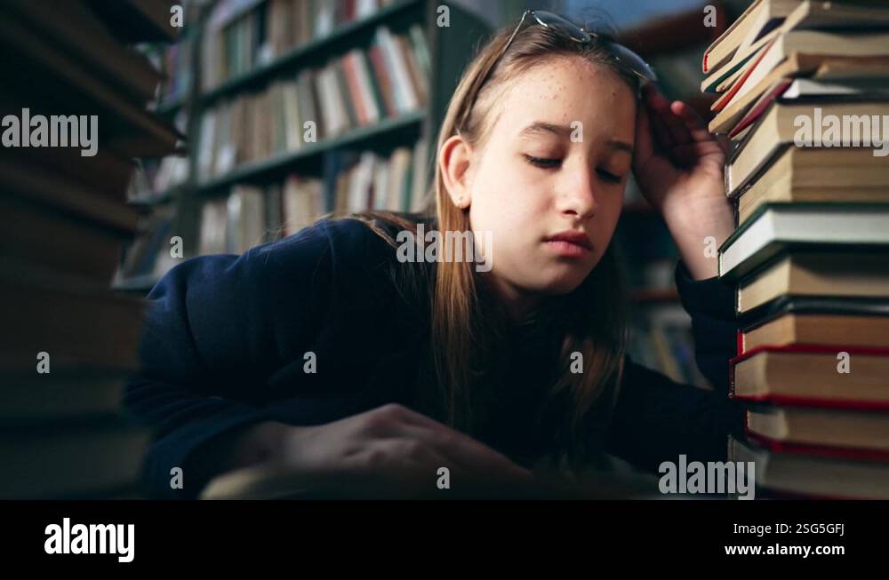Girl in library between the bookshelves and reading book aloud for ...