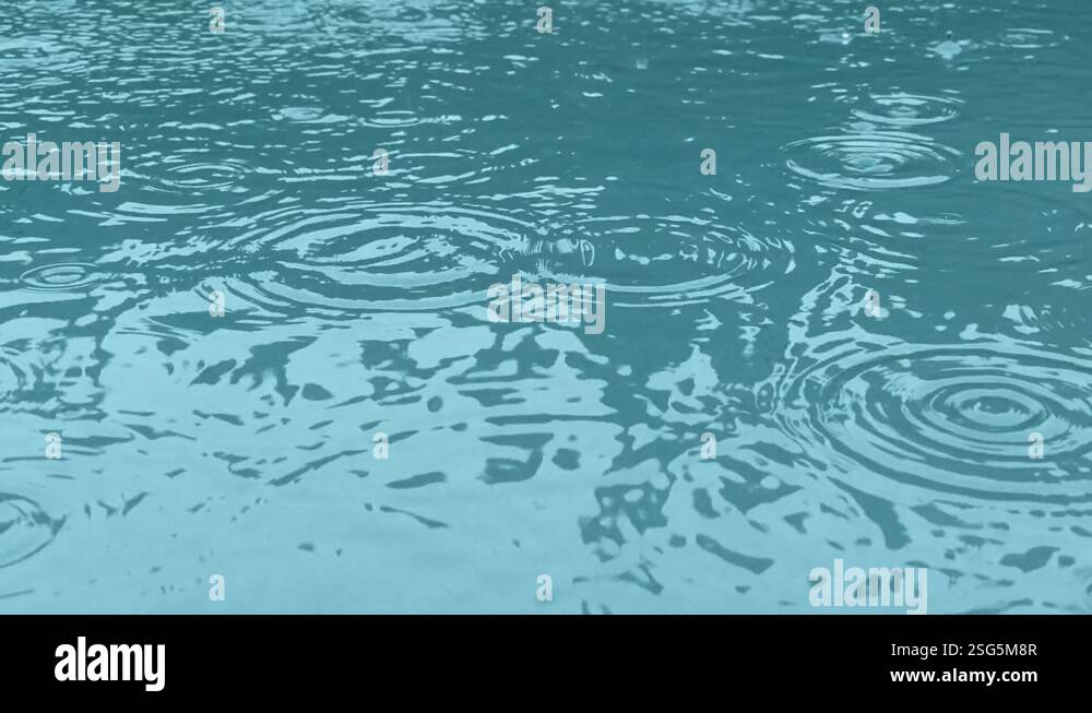 Rain drops splashing into clean pool of aquamarine water, close up slow ...