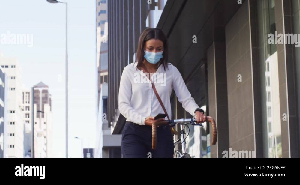 African american woman wearing face mask using smartphone wheeling ...