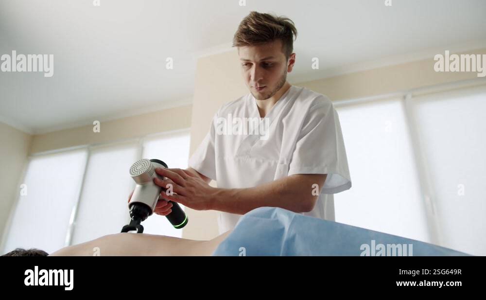 Doctor treating the patients back muscles with massaging percussion ...