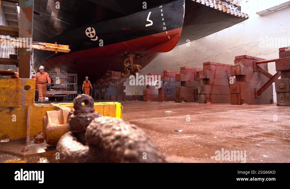 Ship in drydock with yard workers in coveralls walking below hull Stock ...