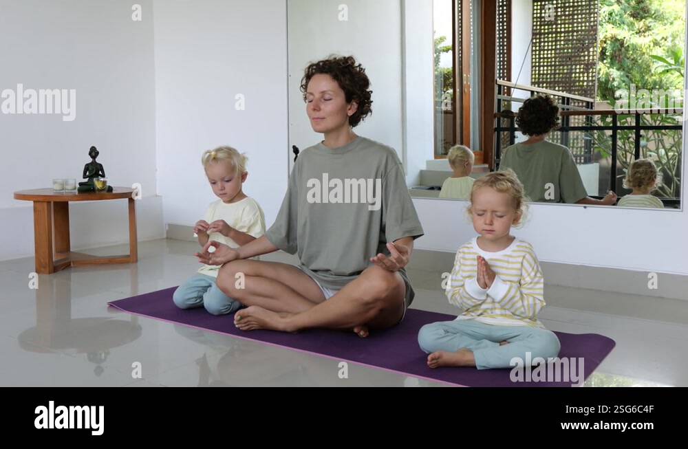 Mom and daughters sit in the lotus position on the rug with their eyes ...