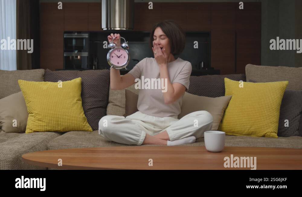 Time for a nap. Tired yawning young girl holding alarm clock, showing ...