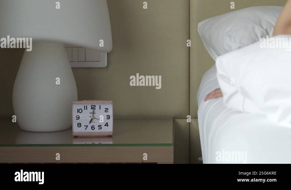 Woman turns off ringing alarm clock on table after waking up Stock ...
