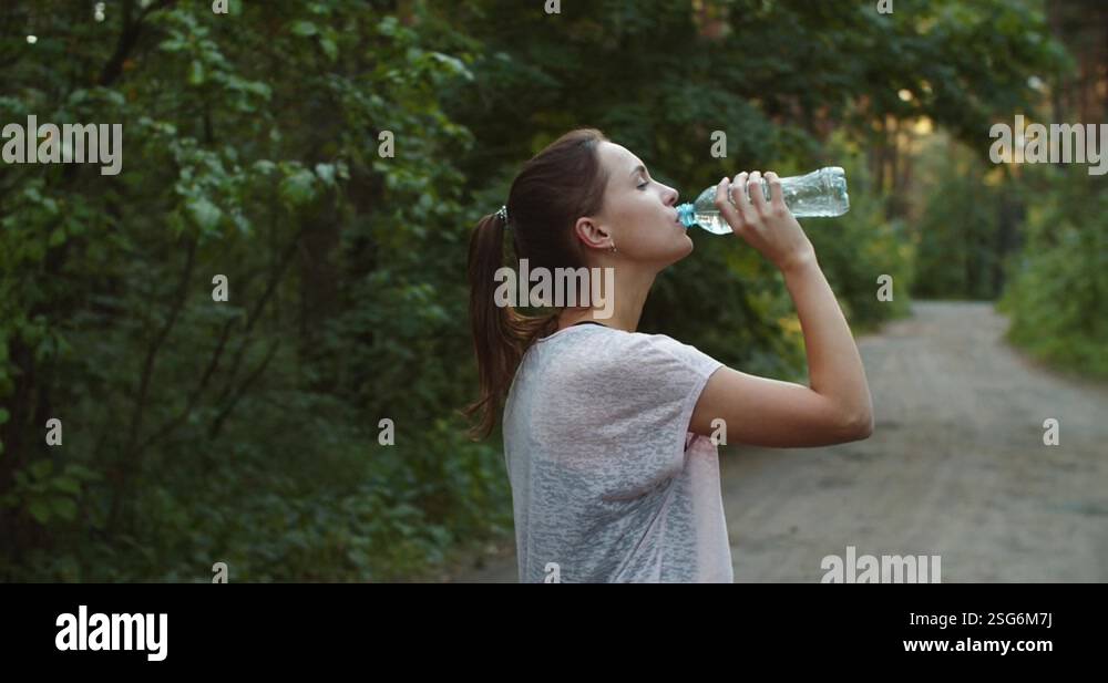 Young woman athlete takes a break, drinking water, out on a run on a ...