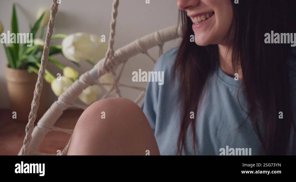 Attractive female laughing while relaxing in swinging chair in living ...