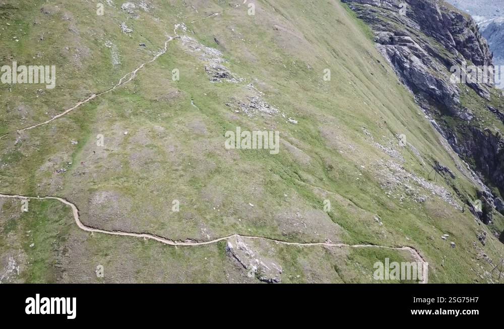 Grass field in the Swiss alps, mountain path for walkers and downhill ...