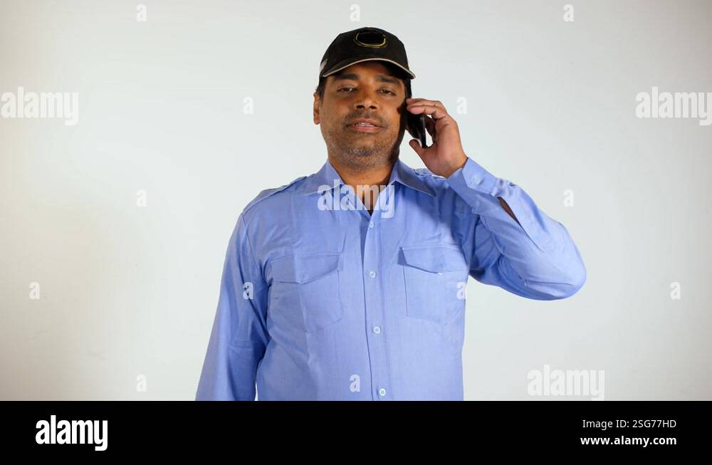 A middle-aged security guard with stubble talking on his smartphone ...