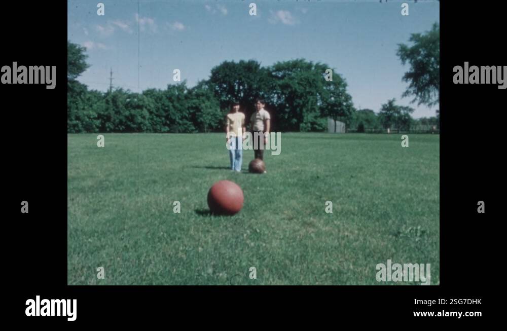 1970s: Balls in grass, zoom out, feet kick ball. Ball rolls from kids ...