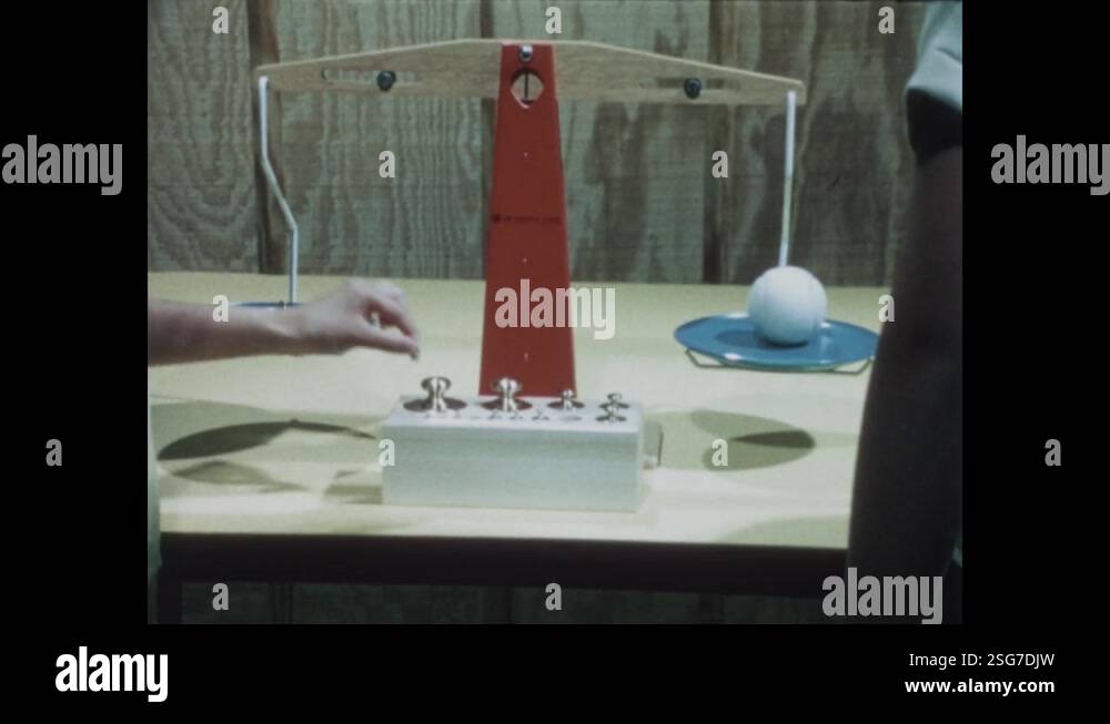 1970s: Hand puts weight on scale. Close up, scale moving. Balanced ...