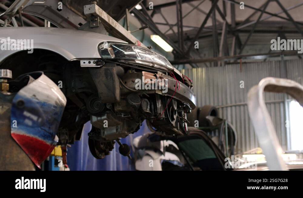 gray passenger car without front bumper hangs on lift in service area ...