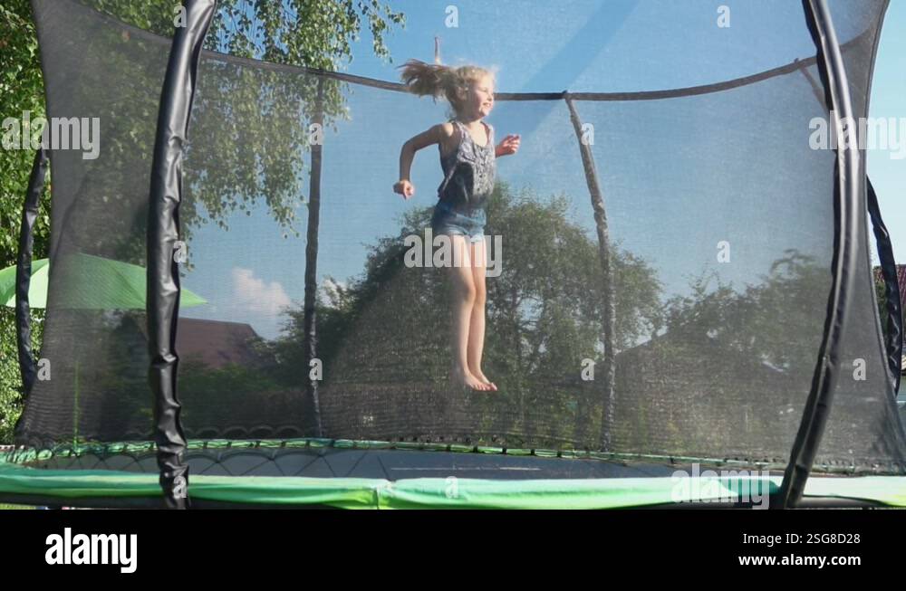 A cute little girl in a jeans shorts is jumping and having fun on the ...