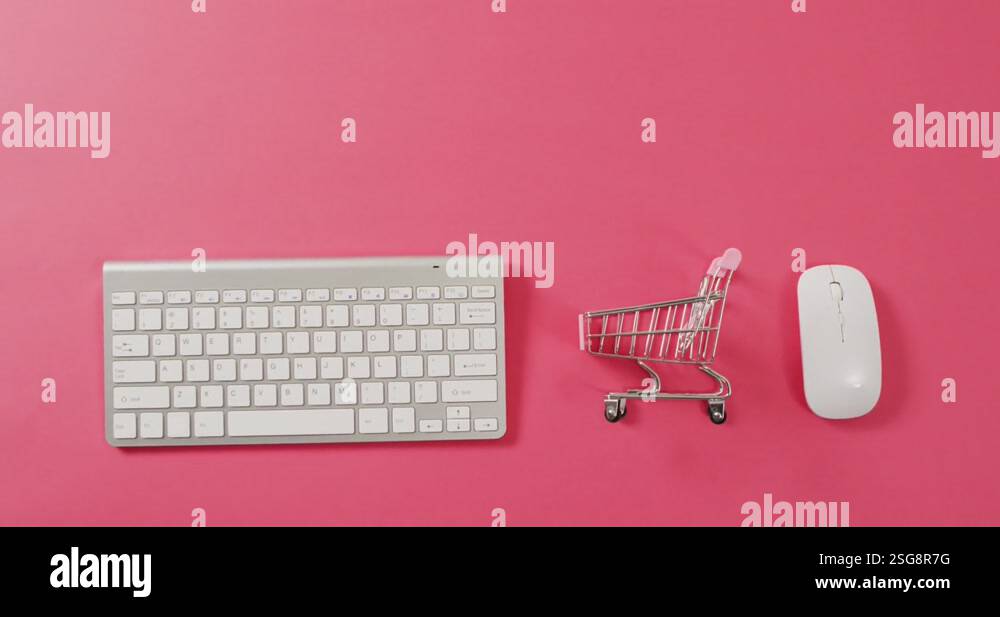 Overhead view of computer keyboard, shopping trolley and mouse on pink ...