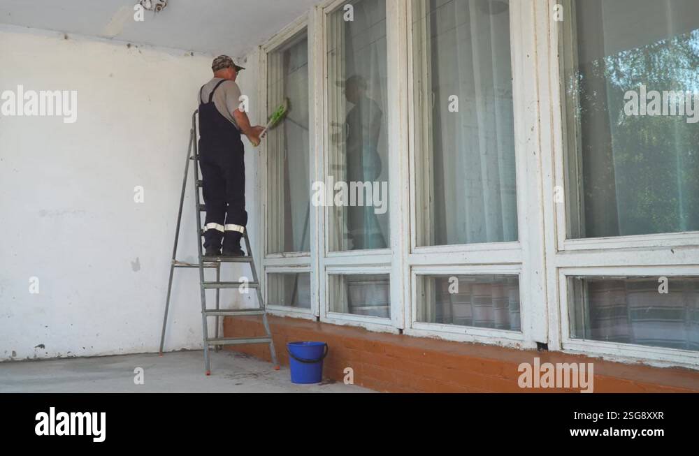 A man window cleaner on a stepladder washes the window with rag on a ...