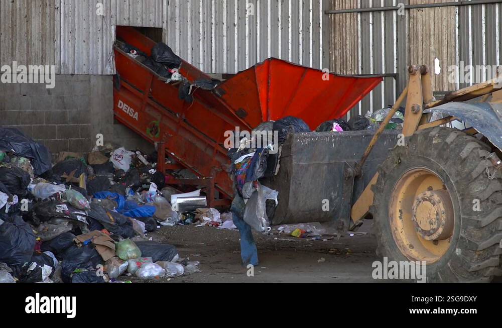 A bulldozer approaches a conveyor belt to dump garbage inside a waste ...