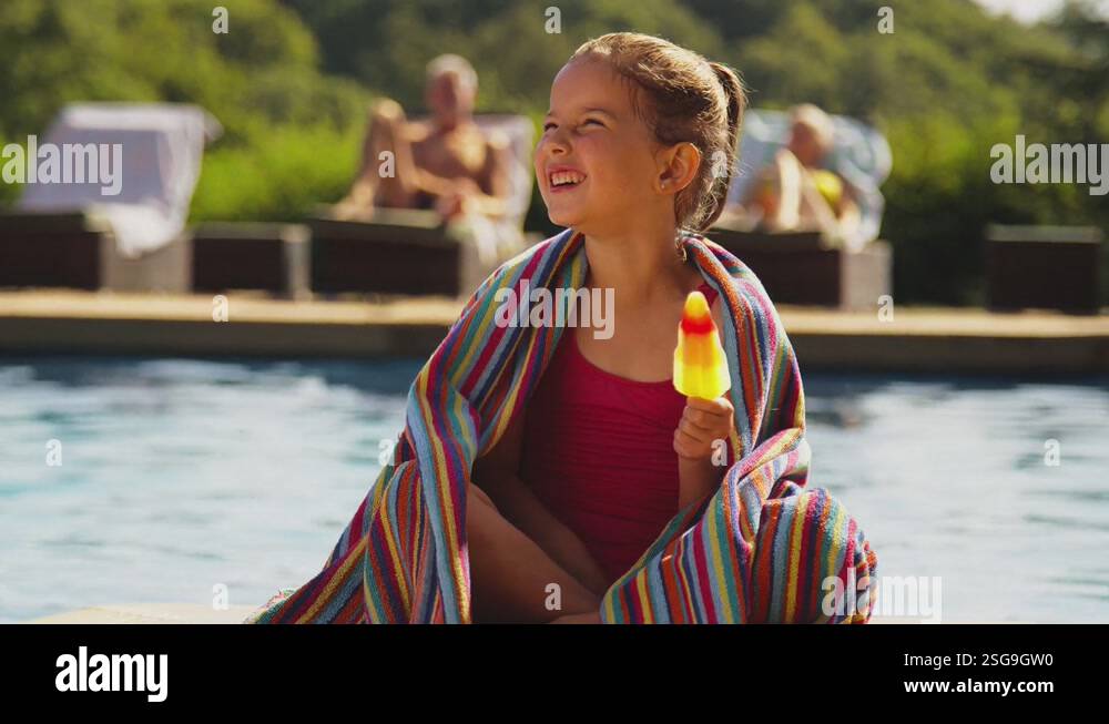 Family On Summer Holiday With Girl Eating Ice Lolly At Edge Of Swimming ...