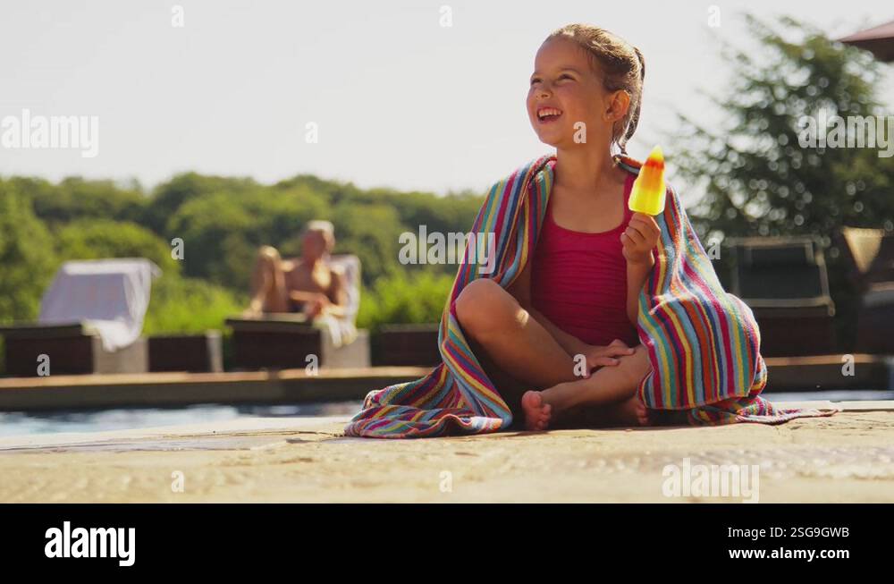 Family On Summer Holiday With Girl Eating Ice Lolly At Edge Of Swimming ...