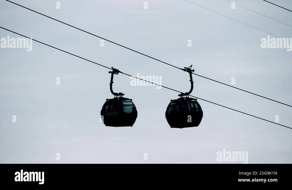 Ropeway, cable car cabins silhouettes are moving against gray sky in ...