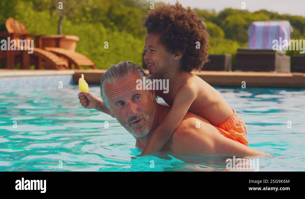 Grandfather Playing With Grandson Eating Ice Lolly In Swimming Pool On ...